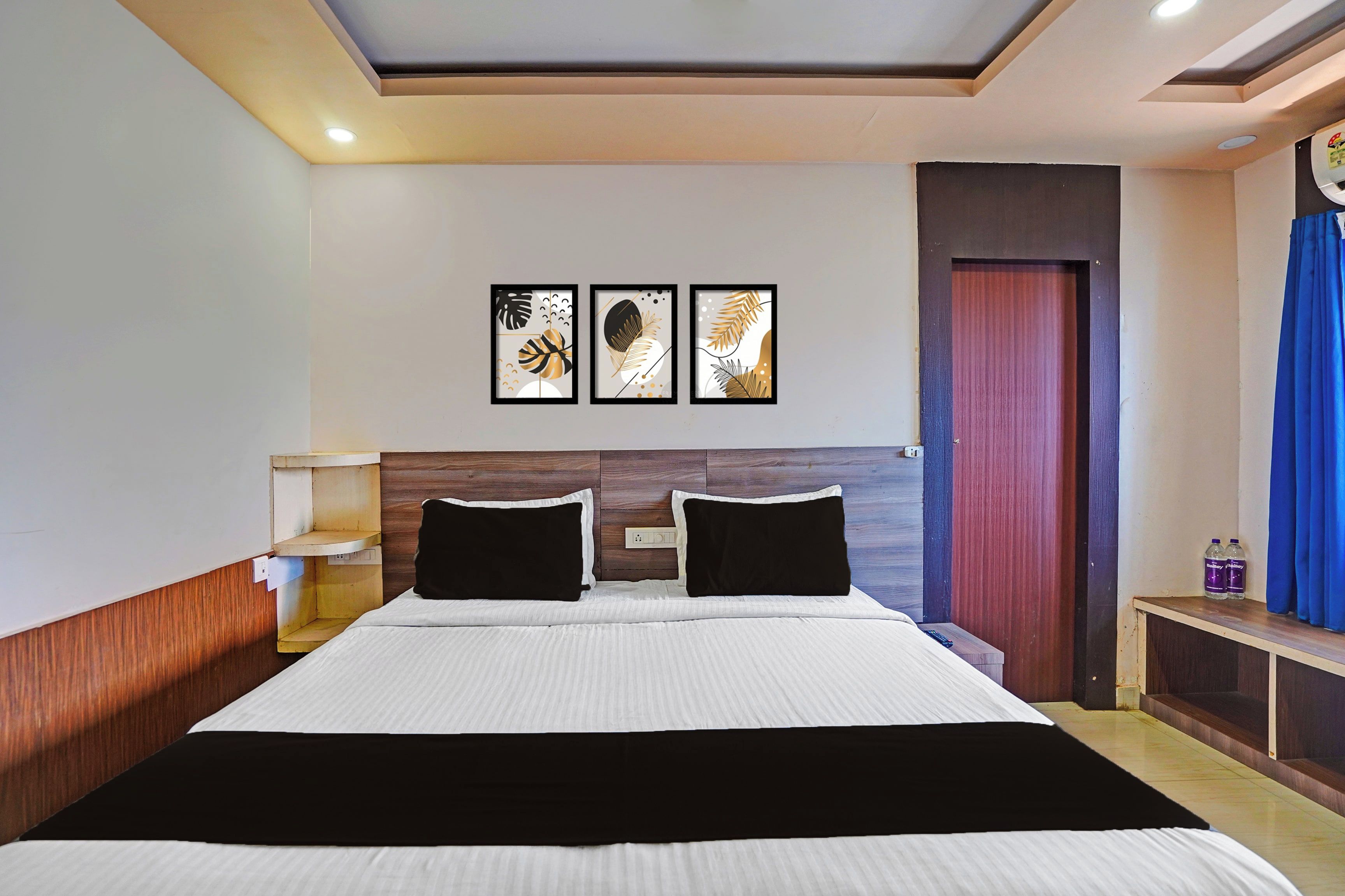 Quarto de hotel com cama, duas mesas de cabeceira, uma mesinha de apoio, uma luminária na parede e uma porta.