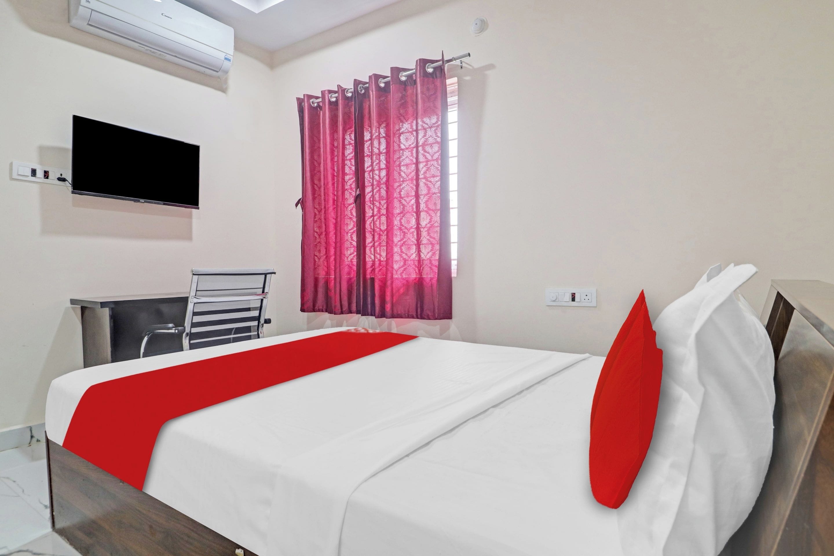 Quarto de hotel com cama, televisão na parede, janela com cortinas e porta-toalhas.