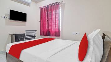 Quarto de hotel com cama, televisão na parede, janela com cortinas e porta-toalhas.