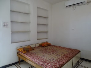 Quarto com cama, estante fixa na parede e aparelho de ar condicionado.