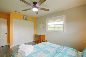 Quarto com cama, ventilador de teto, janela com persianas, guarda-roupa e uma pequena mesa.
