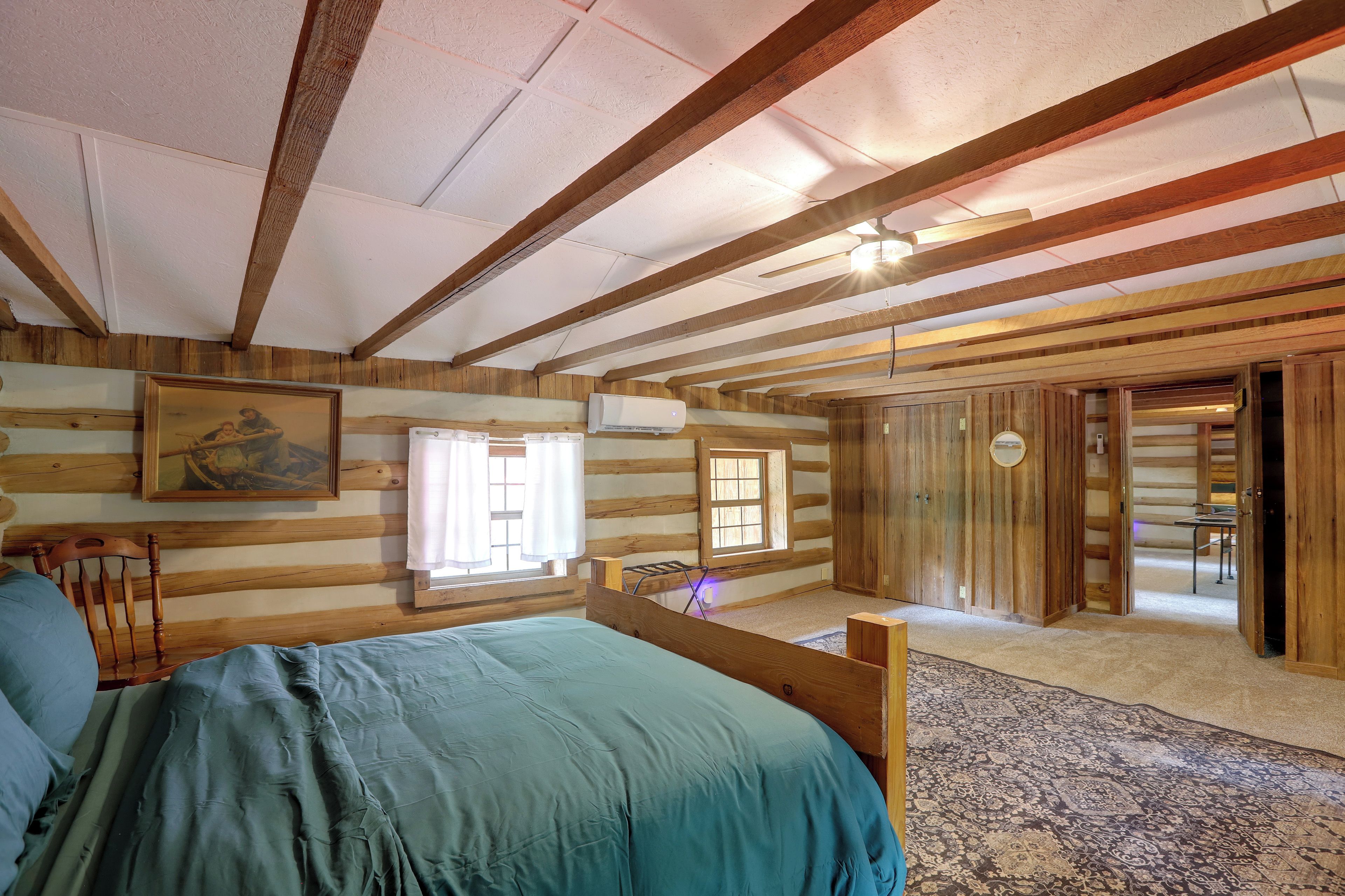 Quarto de cabana de tronco com uma cama, duas janelas, uma porta e um espelho.