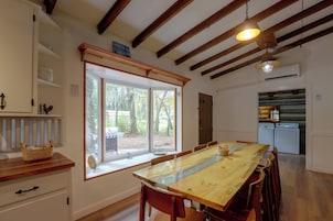 Uma sala de jantar com uma grande mesa de madeira, cadeiras e janela com vista para o exterior.