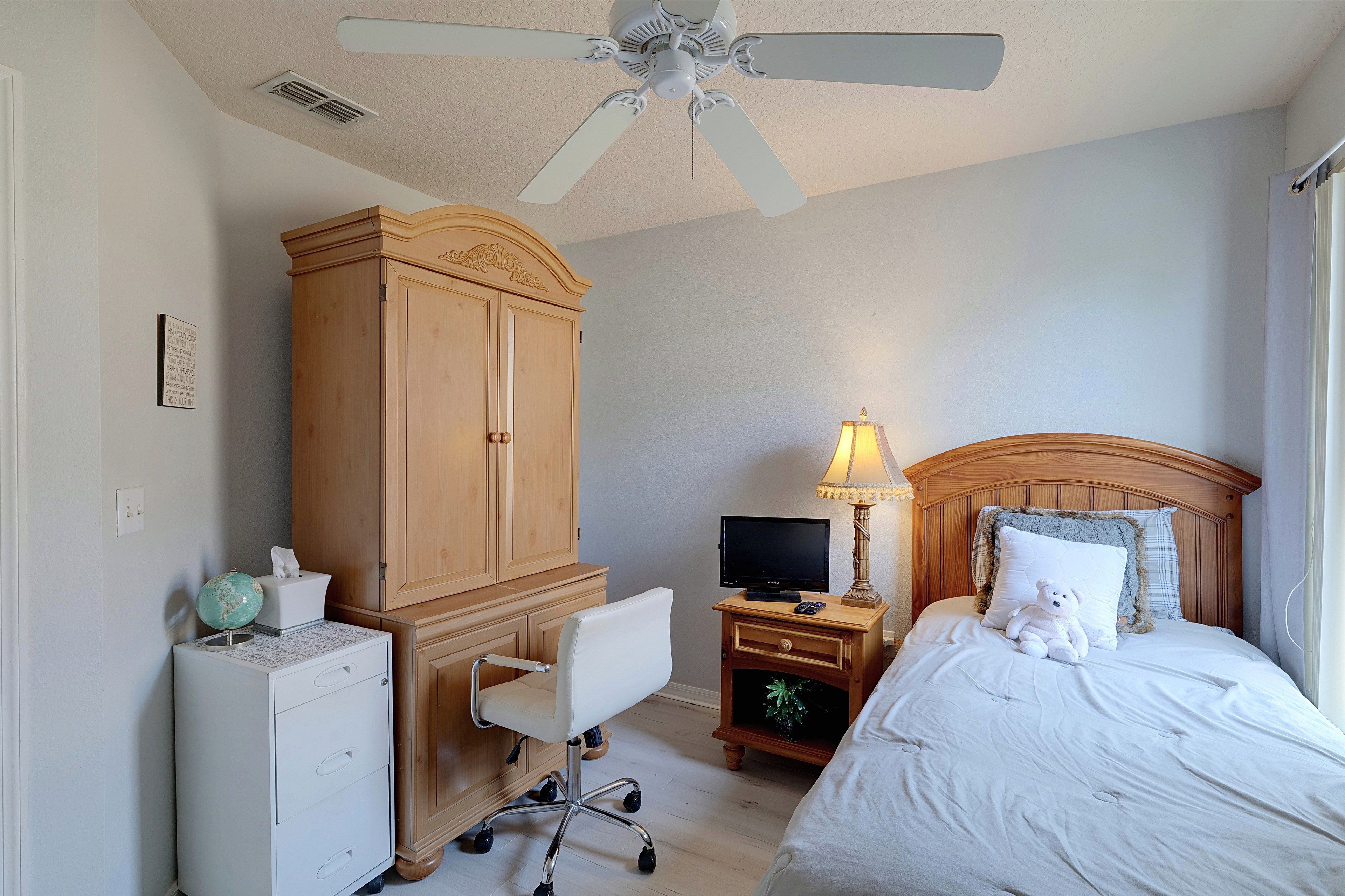 Quarto com cama, escrivaninha, guarda-roupa, televisão e luminária.