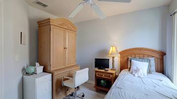 Quarto com cama, escrivaninha, guarda-roupa, televisão e luminária.