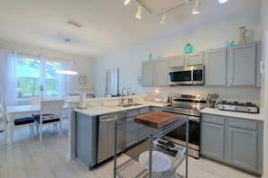 Cozinha moderna com ilha central, eletrodomésticos de aço inoxidável e área de refeições com mesa e cadeiras.