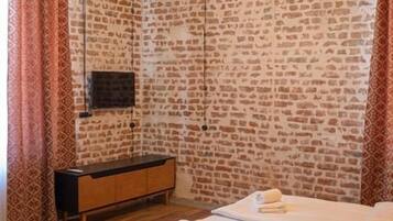 Quarto com parede de tijolos, cama com cabeceira de madeira, um banco de madeira e duas luminárias pendentes.