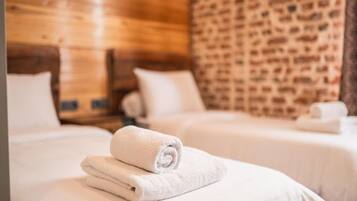Quarto de hotel com duas camas, cada uma com uma toalha branca dobrada. O quarto tem paredes de madeira e uma parede de destaque com padrão de tijolos.