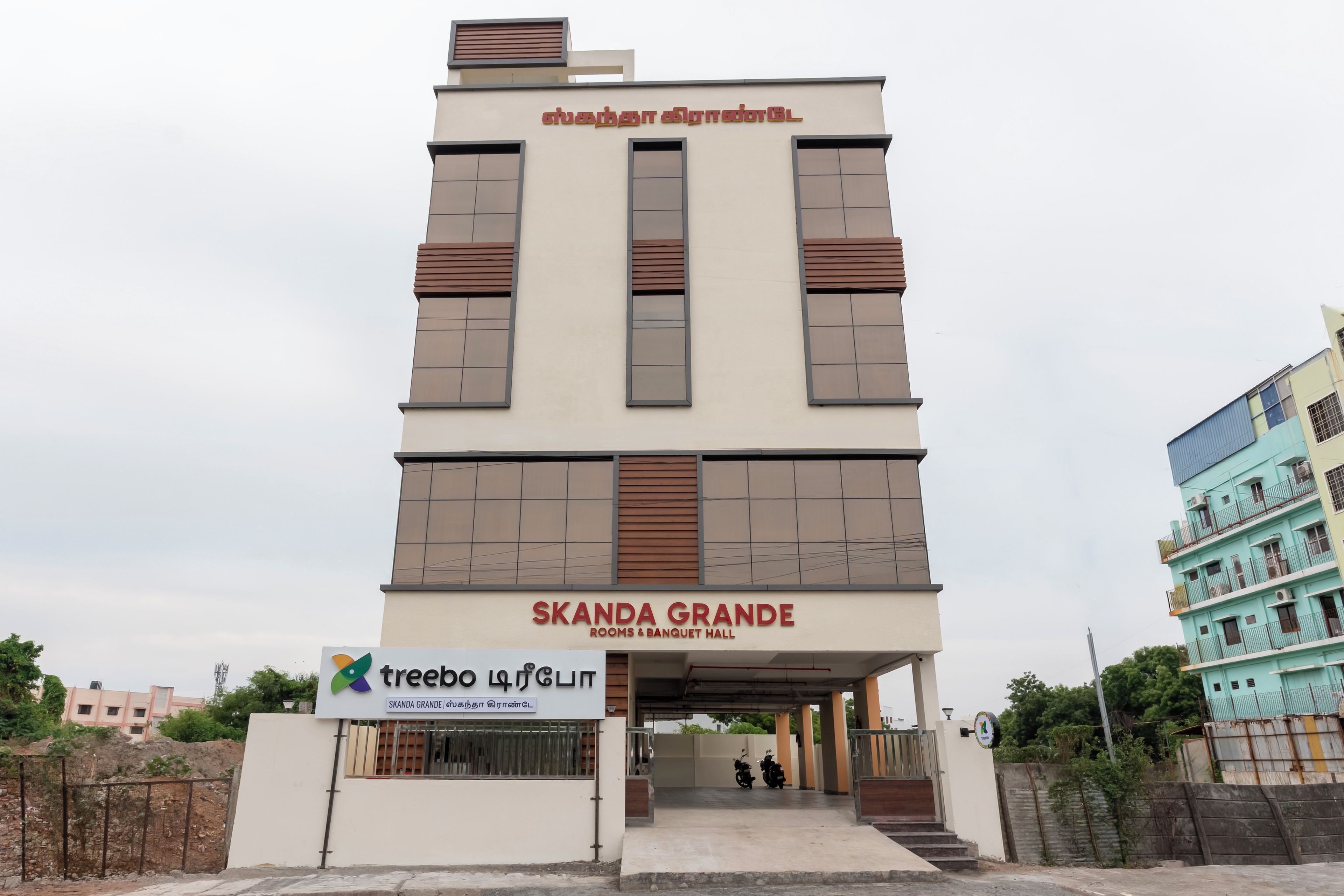 Um edifício de vários andares com uma placa indicando 'SKANDA GRANDE ROOMS & BANQUET HALL'.