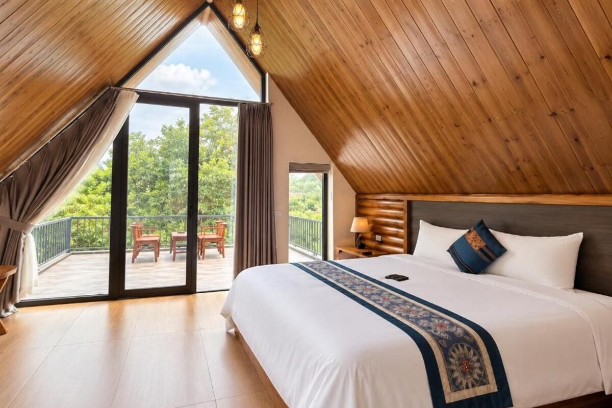 Quarto com cama grande, teto de madeira e vista para o exterior.