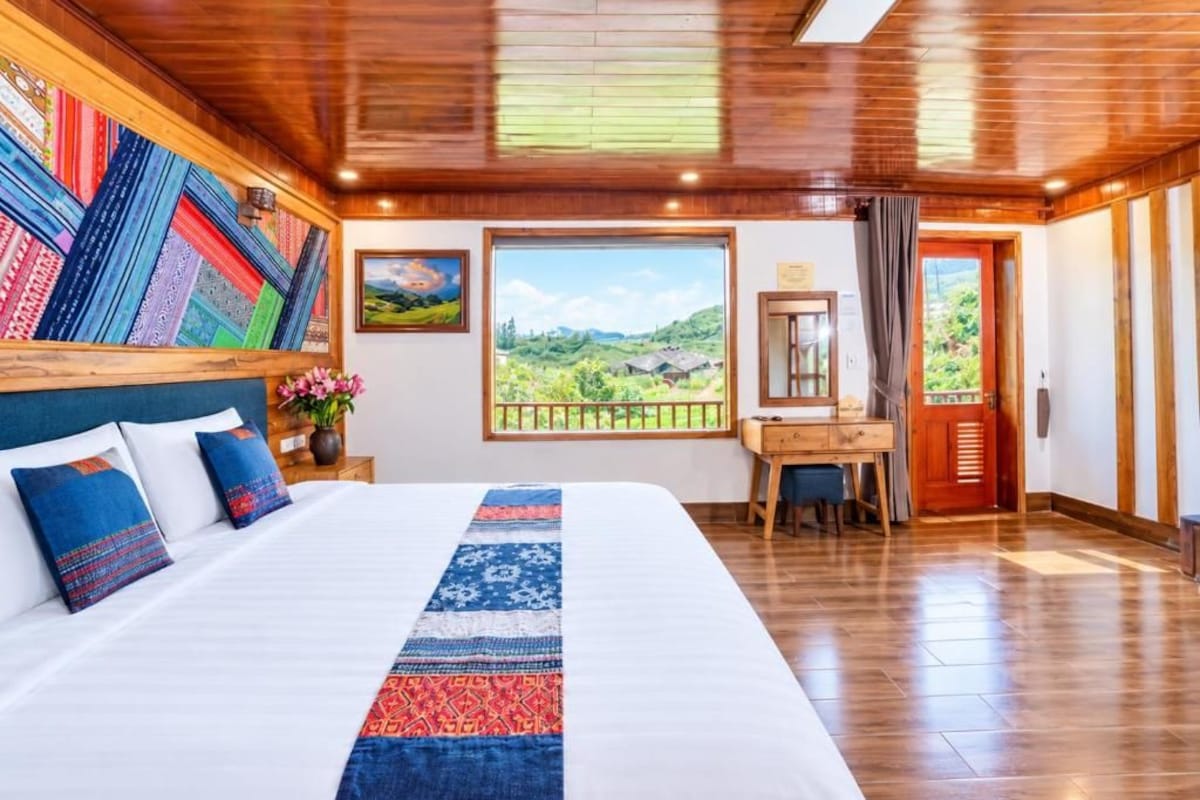 Quarto espaçoso com uma cama grande, uma escrivaninha de madeira e vista para uma paisagem verde pela janela.