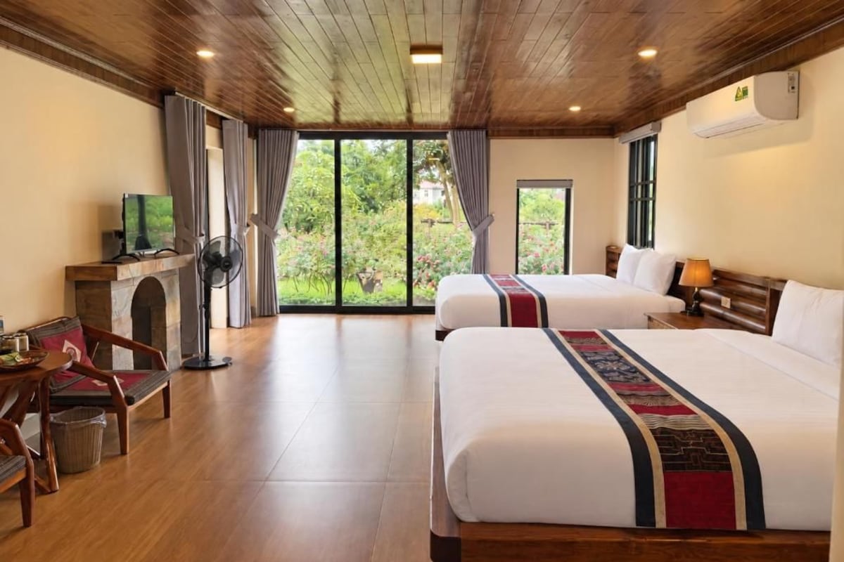 Quarto de hotel com duas camas, televisão, lareira e vista para o verde.