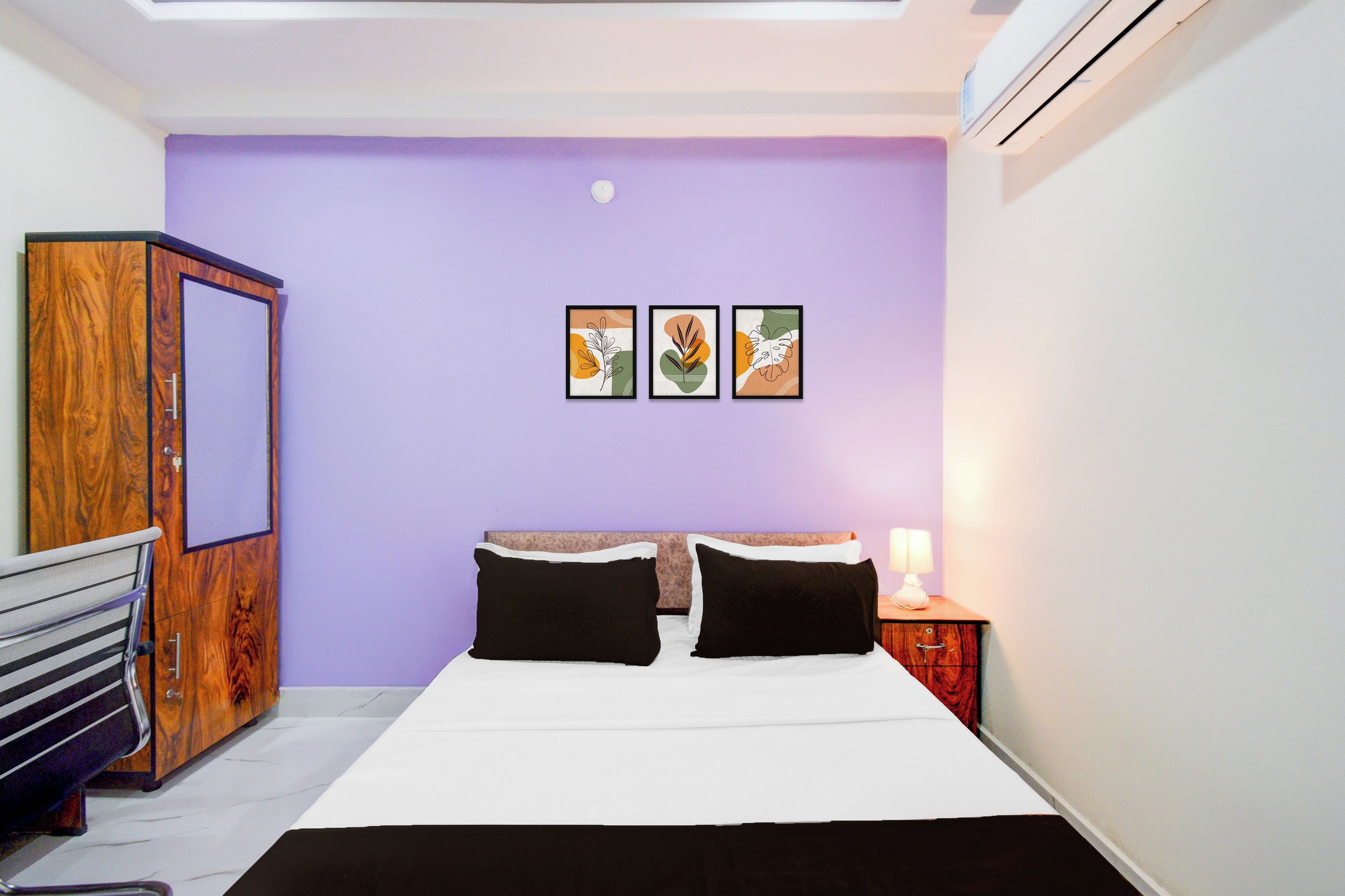 Quarto com cama, duas almofadas, mesa de cabeceira com abajur, guarda-roupa e três quadros na parede.