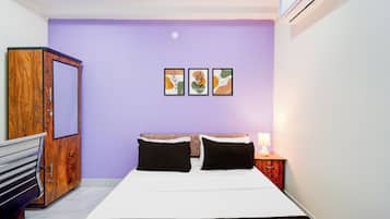 Quarto com cama, duas almofadas, mesa de cabeceira com abajur, guarda-roupa e três quadros na parede.