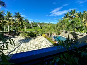 Área de piscina com piso de azulejos, rodeada por vegetação exuberante e palmeiras.