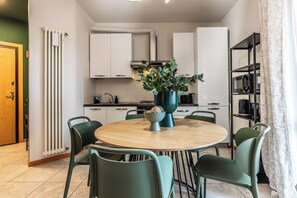 Cozinha moderna com armários brancos, mesa redonda de madeira e cadeiras verdes.