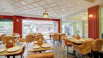 Espaço de refeições de hotel com mesas para quatro pessoas, cadeiras e um candelabro.