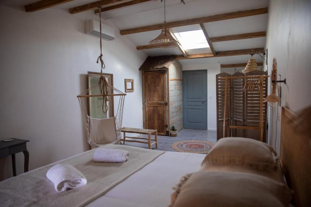 Quarto com cama, cadeira suspensa, guarda-roupa de madeira e porta que dá para outro cômodo.