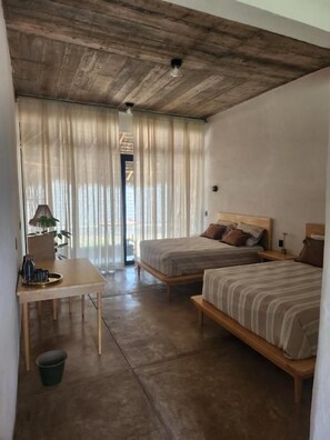 Quarto com duas camas, uma mesinha e um ventilador de teto.