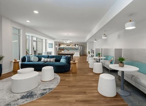 Sala de estar moderna com sofá, pufes e cozinha ao fundo.