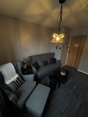 Uma sala de estar moderna com um sofá cinza, uma mesinha e uma luminária pendente em formato de estrela.