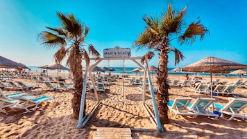 Uma praia com espreguiçadeiras, palmeiras e um aviso indicando 'Marin Beach Hotel'.