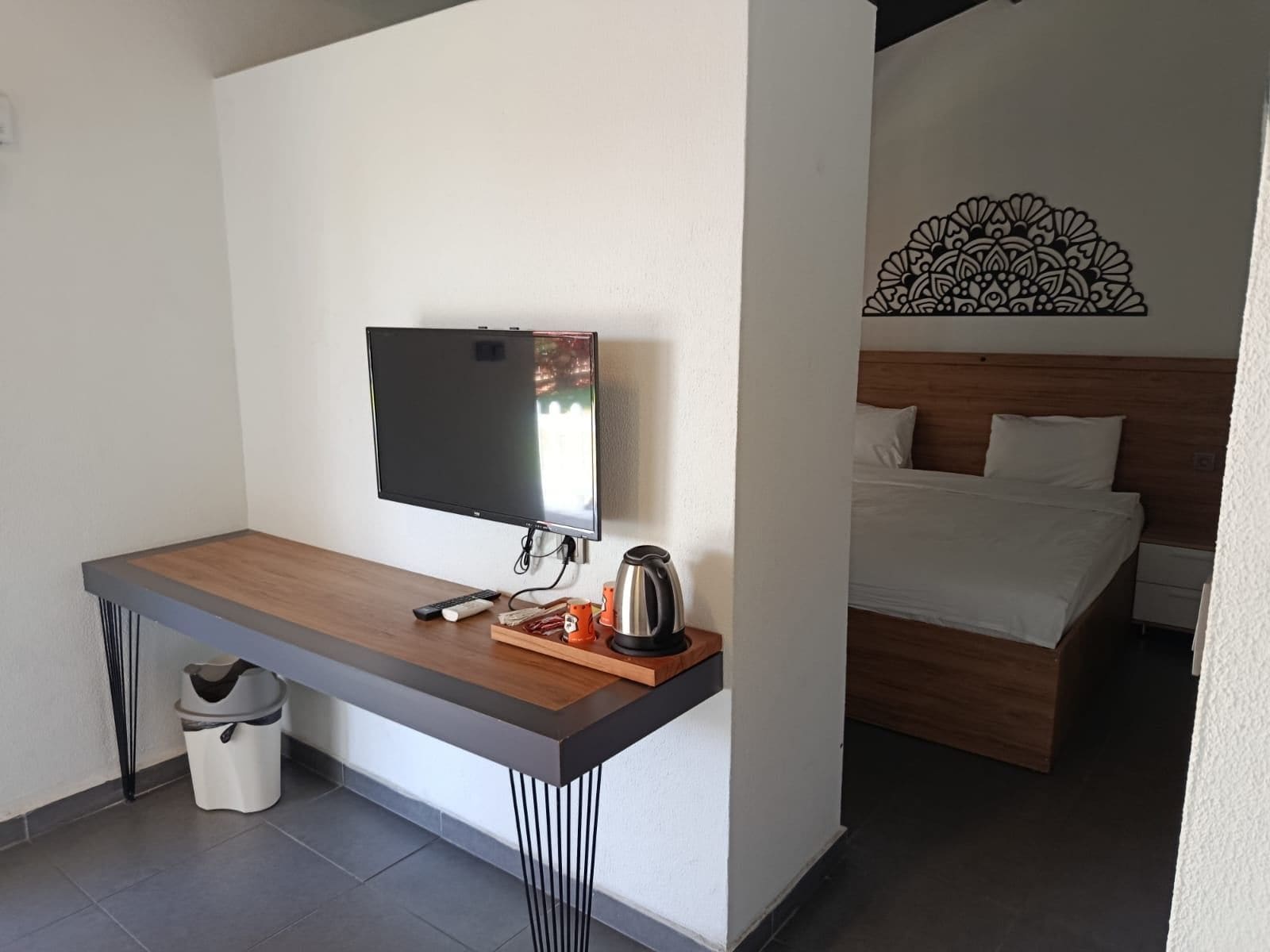 Quarto com cama, escrivaninha com televisão, cafeteira e lixeira.