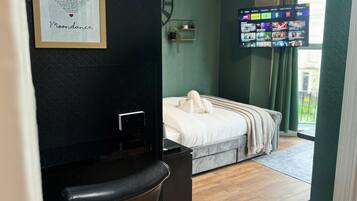 Quarto de hotel com cama, escrivaninha, cadeira, televisão presa à parede e janela com cortinas.