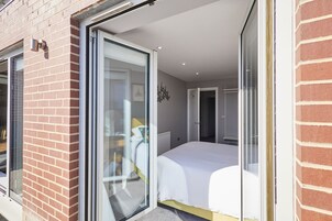 Quarto com cama, porta de correr de vidro que dá para uma varanda e parede externa de tijolos.