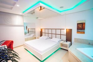 Quarto moderno com uma cama grande, mesas de cabeceira, uma cadeira vermelha, um espelho e um banheiro com banheira.