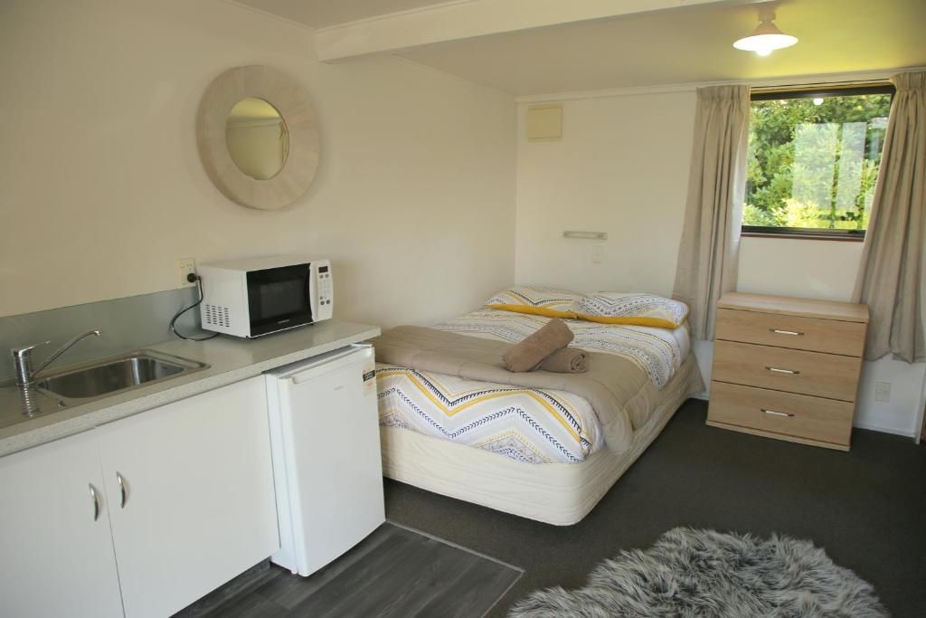 Quarto compacto com cozinha compacta, cama com roupa de cama estampada, um pequeno espelho redondo e uma janela com cortinas.