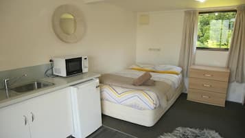 Quarto compacto com cozinha compacta, cama com roupa de cama estampada, um pequeno espelho redondo e uma janela com cortinas.