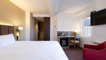 Quarto de hotel com cama, escrivaninha, cadeira e televisão.