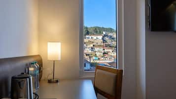 Quarto de hotel com vista para uma cidade, uma mesa com abajur, uma cadeira e uma TV na parede.