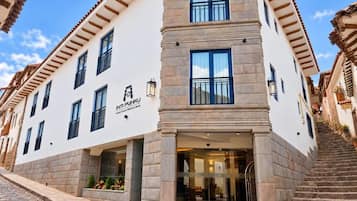 Hotel com fachada branca, várias janelas e escadaria que leva à entrada.