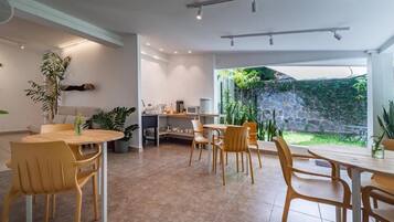 Uma área de refeições moderna com cozinha ao fundo, uma grande janela com vista para o verde e um teto com iluminação embutida.