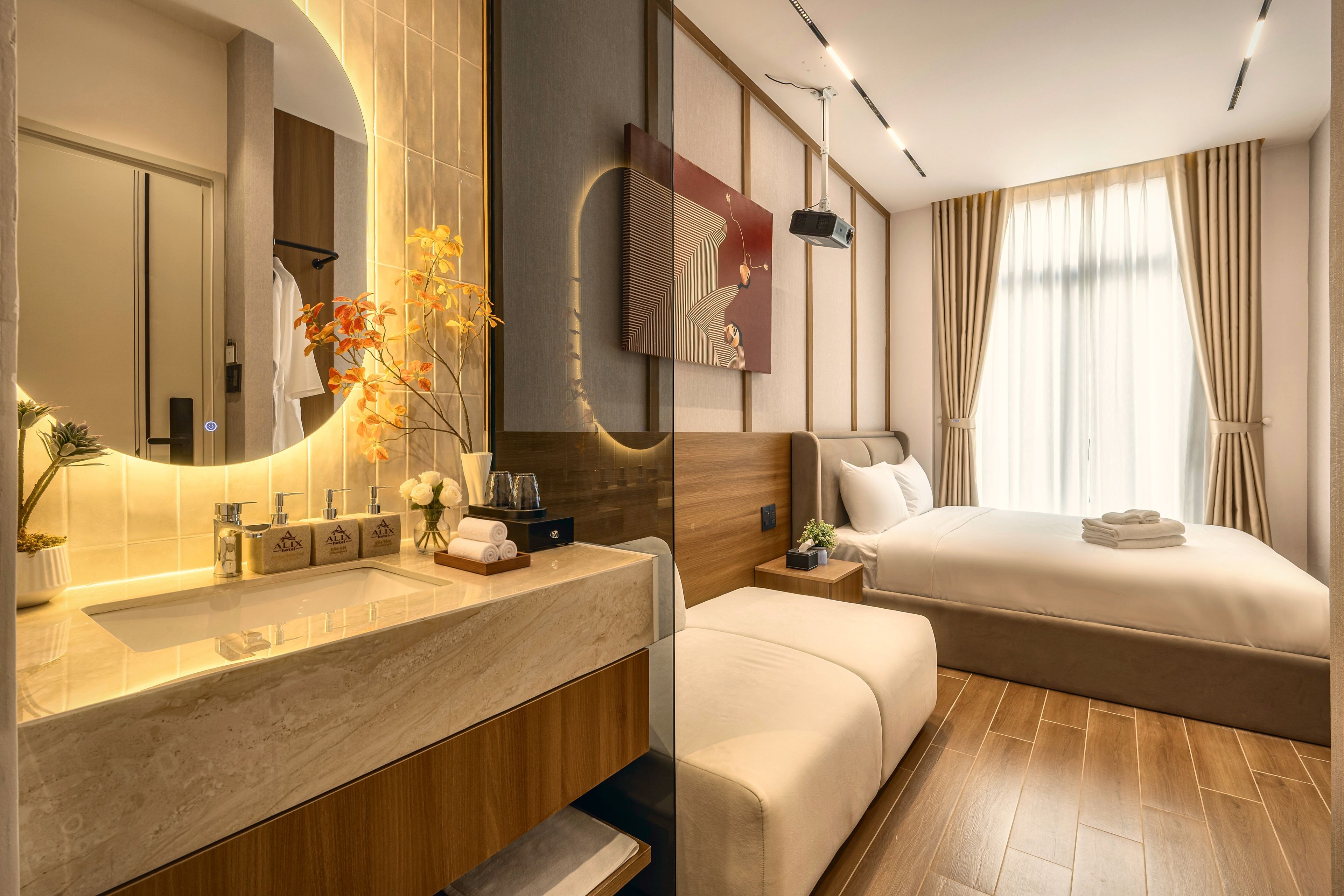 Quarto de hotel moderno com uma cama grande, banheiro com toucador e um espelho amplo.