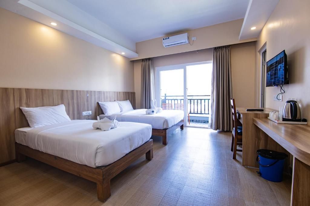 Quarto de hotel com duas camas, uma mesa de trabalho, televisão e varanda.