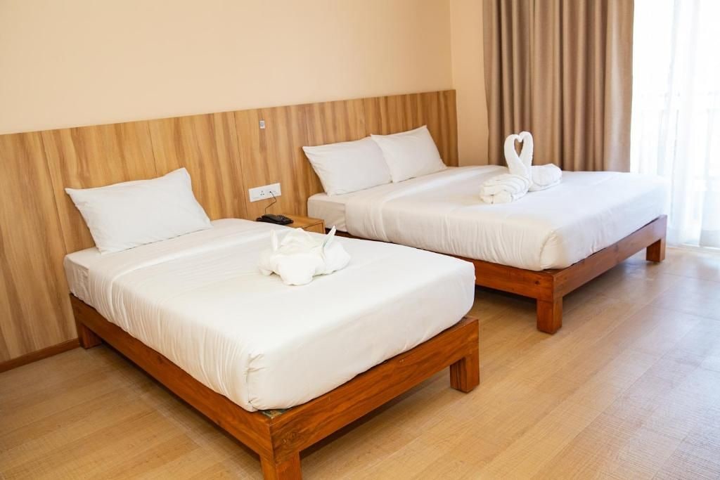 Duas camas de madeira com roupa de cama branca e toalhas em formato de coração, um cabeceira de madeira e piso de madeira.
