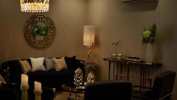 Uma sala de estar moderna com um sofá preto, um painel decorativo redondo, uma mesa com velas e um lustre.