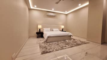 Quarto moderno com cama, mesas de cabeceira, tapete e iluminação embutida no teto.