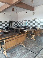 Restaurante com paredes de azulejos quadriculados, mesas e bancos de madeira, e luminárias pendentes.