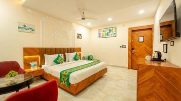 Quarto de hotel com cama, escrivaninha, cadeira, televisão e obras de arte nas paredes.