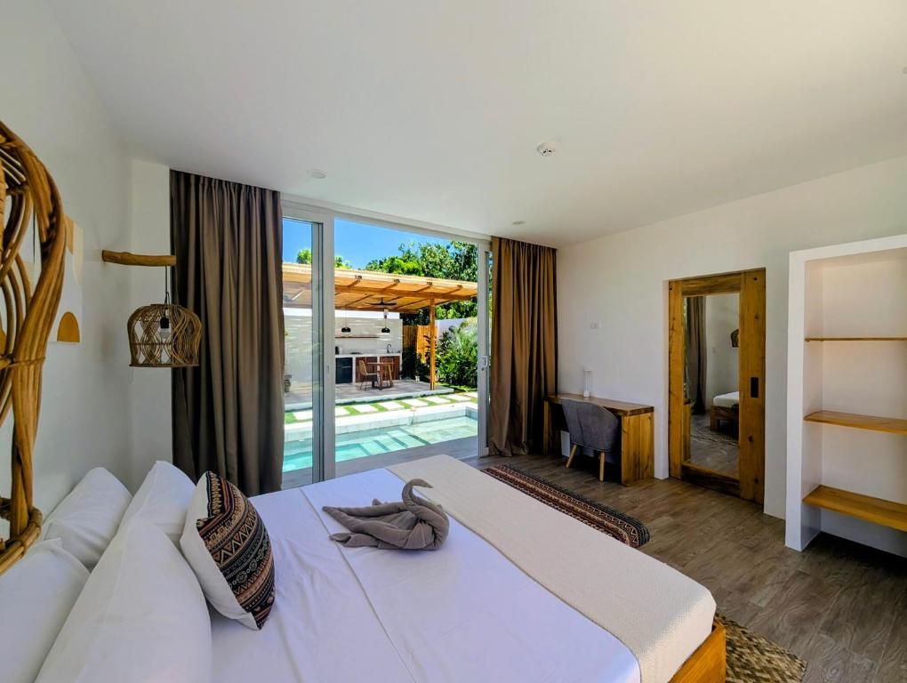 Quarto de hotel com cama, escrivaninha, cadeira e vista para piscina e área externa com assentos.