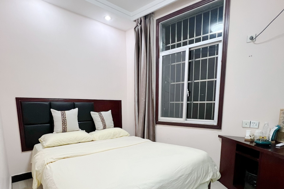 Quarto com cama grande, penteadeira, janela com cortinas e luminária no teto.