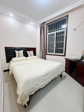 Quarto com cama grande, penteadeira, janela com cortinas e luminária no teto.