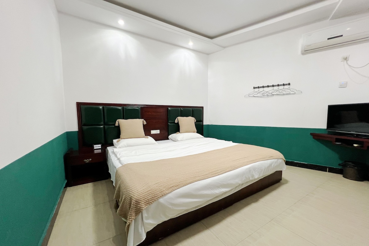 Quarto de hotel com cama, mesas de cabeceira, televisão e ar condicionado.
