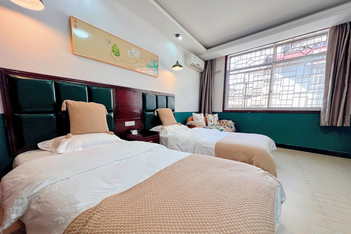 Quarto de hotel com duas camas, uma janela grande com cortinas, ar condicionado fixado na parede e uma luminária no teto.