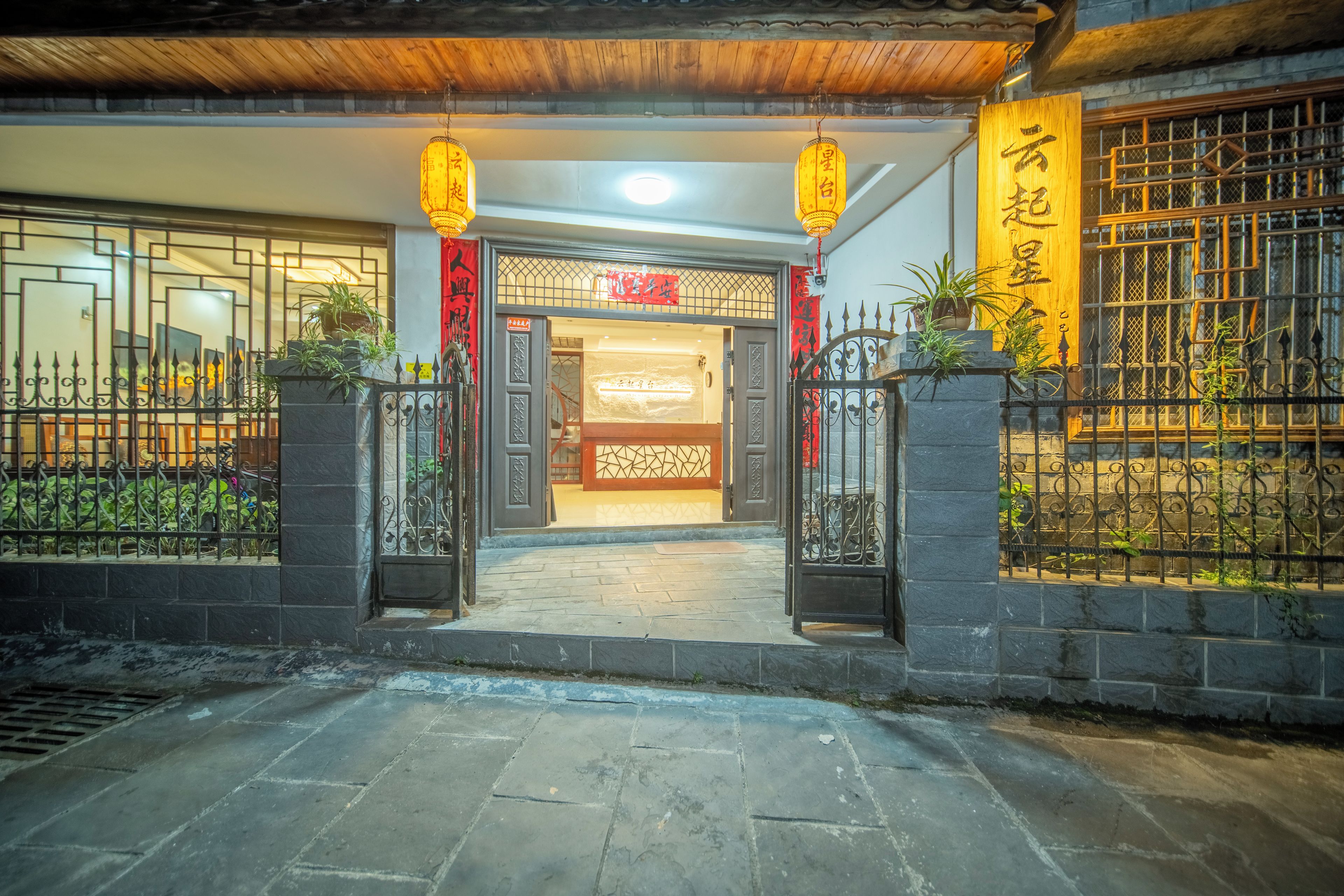 Uma entrada tradicional com portão de madeira, caminho de azulejos e parede decorativa com caracteres chineses.