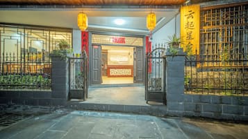 Uma entrada tradicional com portão de madeira, caminho de azulejos e parede decorativa com caracteres chineses.
